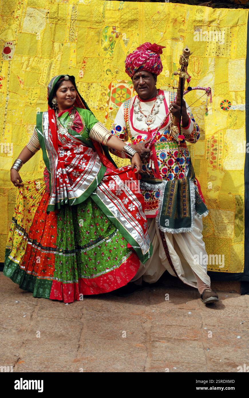 Rajasthani folk musician playing ravanhatta with lady against yellow bedsheets, Jaisalmer ...