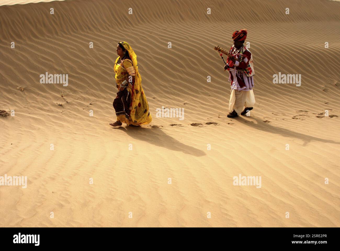 Rajasthani folk musician playing ravanhatta lady walking on sand dune ...