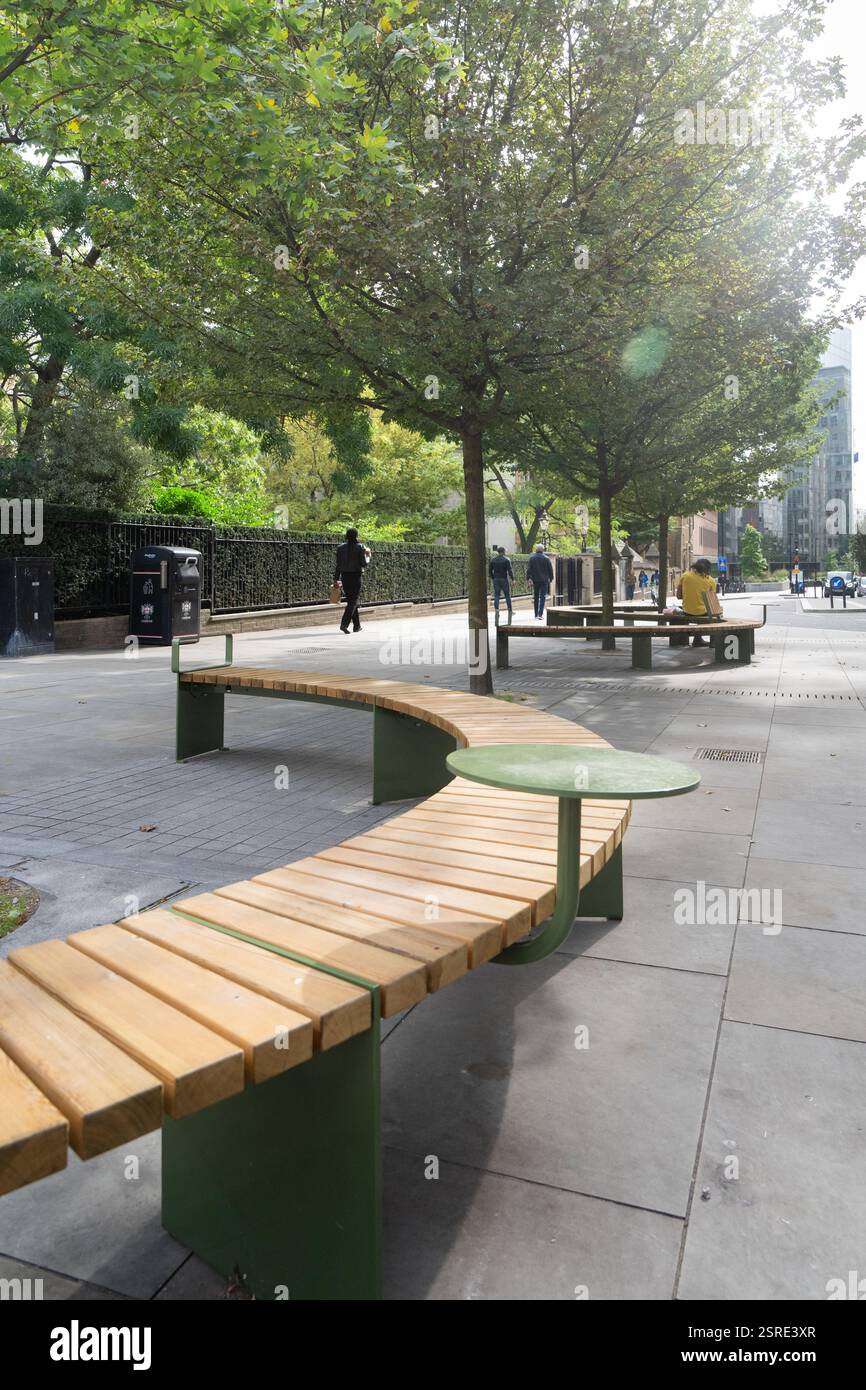 Pedestrians walk past curved park benches. People relax on benches ...
