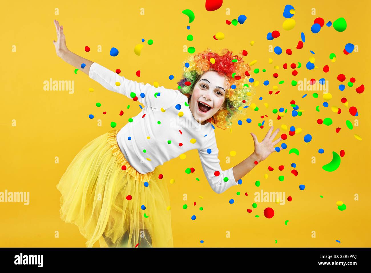 Happy girl dressed like clown under falling confetti on orange ...