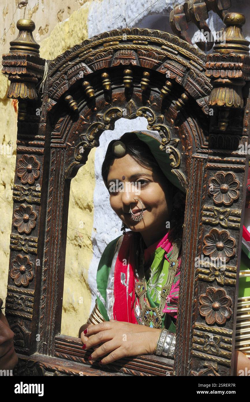 Lady in colourful traditional dress looking through wooden jharoka ...