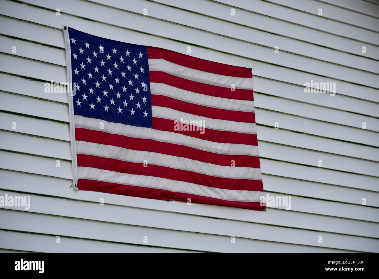 An American flag, a symbol of freedom, displayed on a white clapboard ...