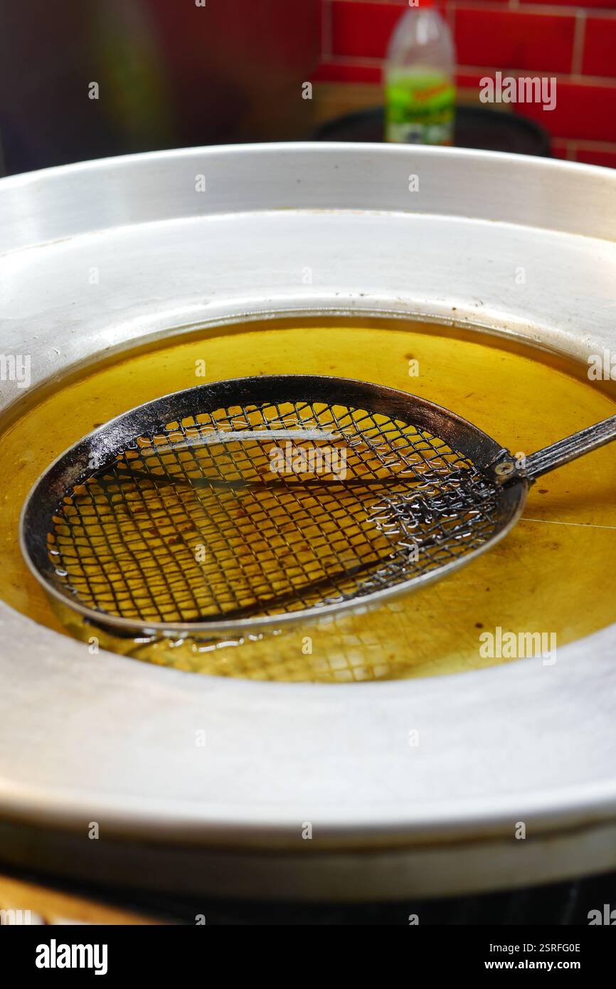 Cooking oil in a deep fryer with a mesh strainer resting inside Stock ...