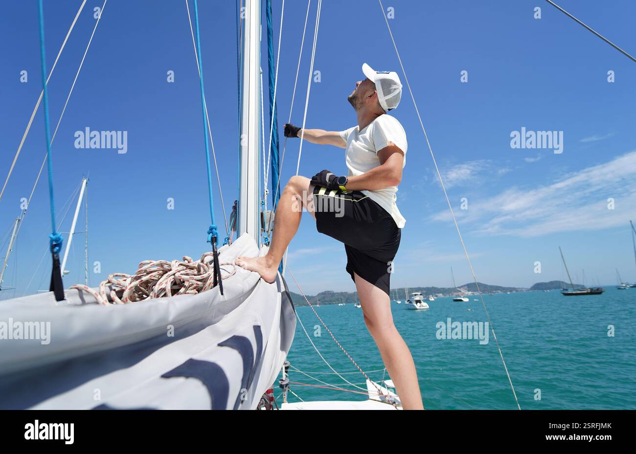 Male captain climbing mast of sailboat to check sails Stock Photo - Alamy