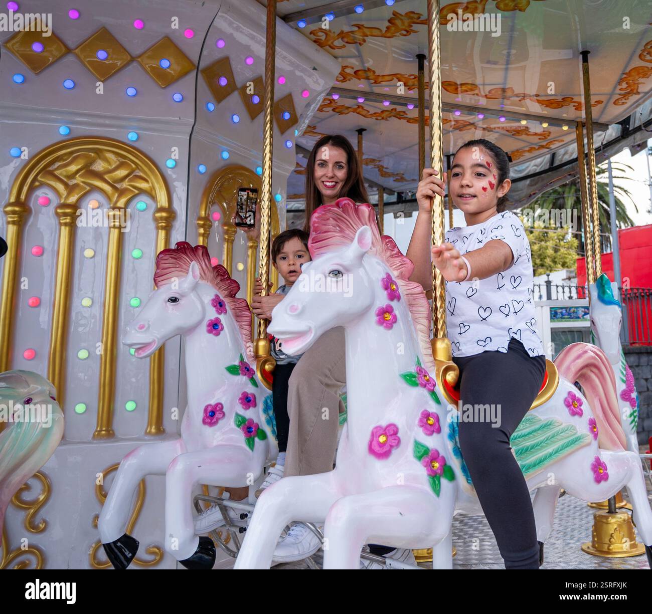 A group of people are riding on a carousel with horses. The carousel is ...