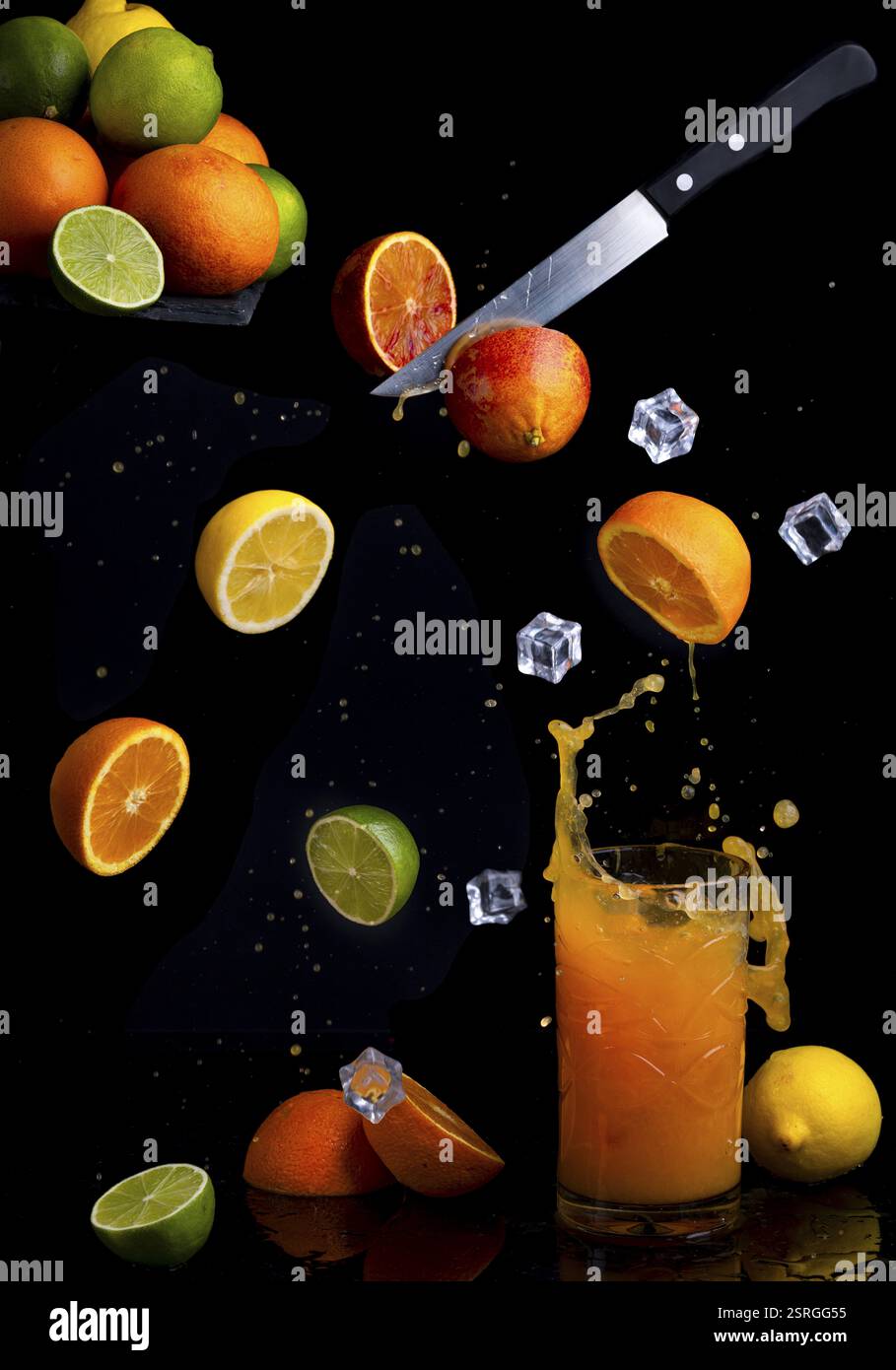 Flying citrus fruits and knives over glass with splashing orange juice ...
