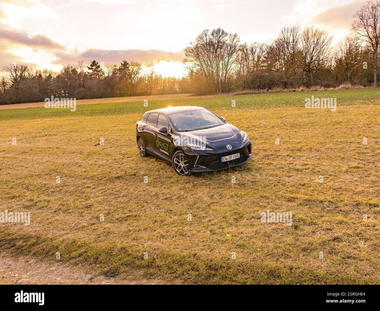 A black car standing alone in a wide field at sunset, e-car sharing ...