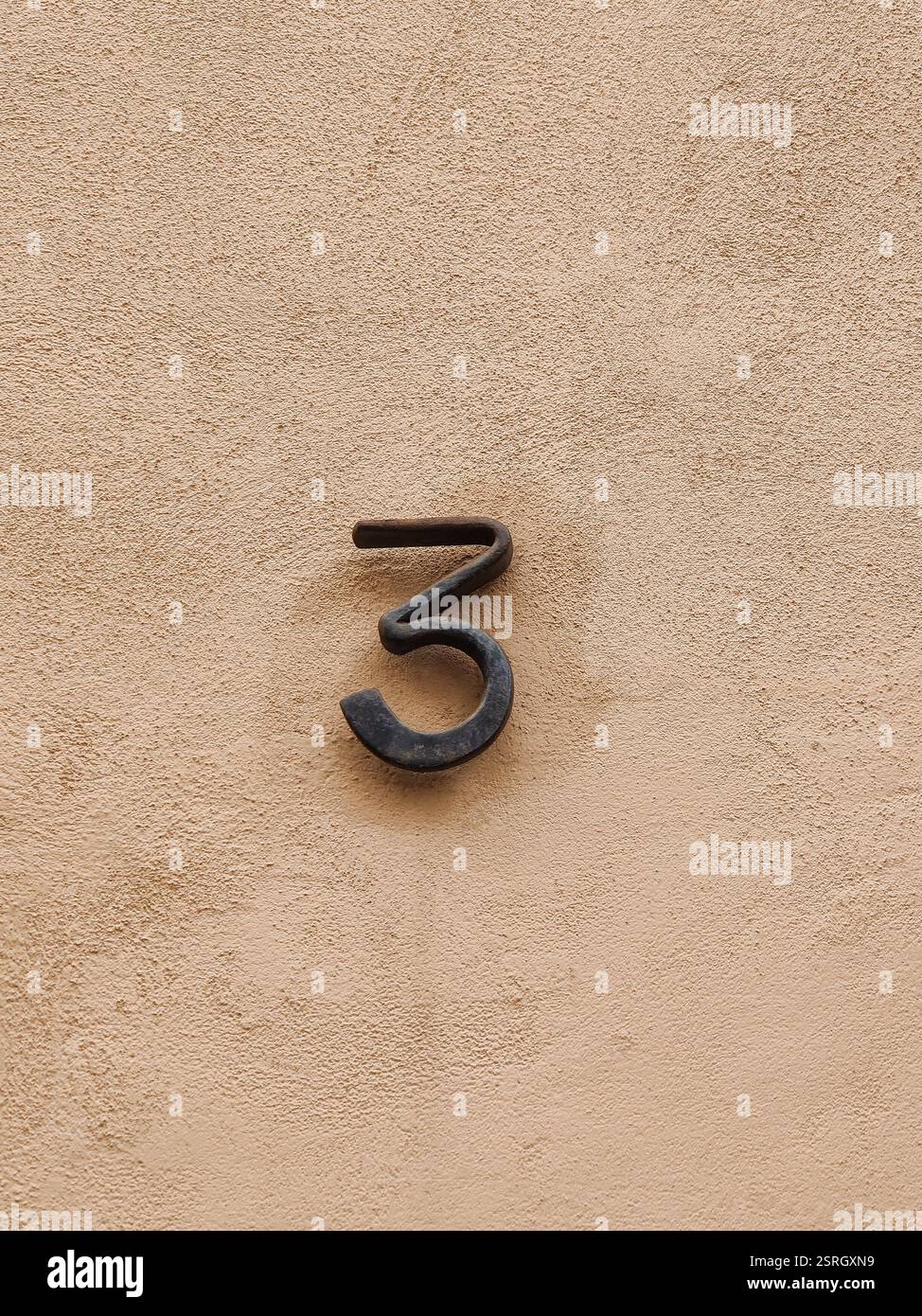 Forged metal number three mounted on pale pink wall. Copy space for ...