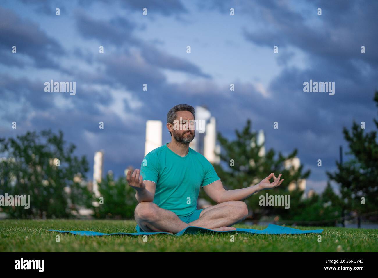 Sport Man meditating in lotus pose in grass outdoors. Sportsman doing ...