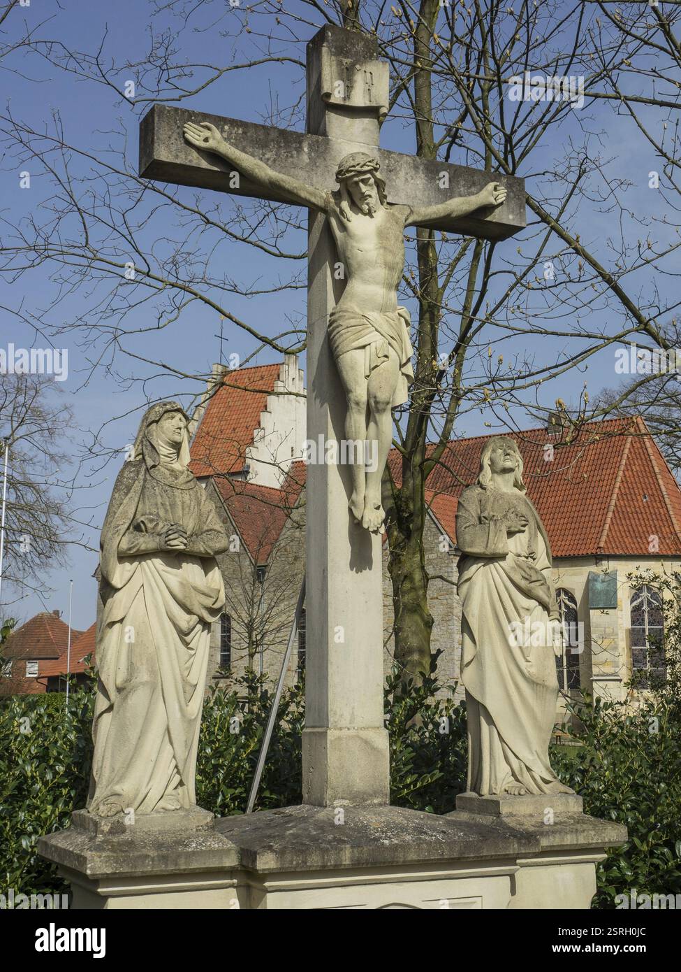 Stone sculptures of the crucifixion of Jesus in front of a church under a blue sky, muensterland ...