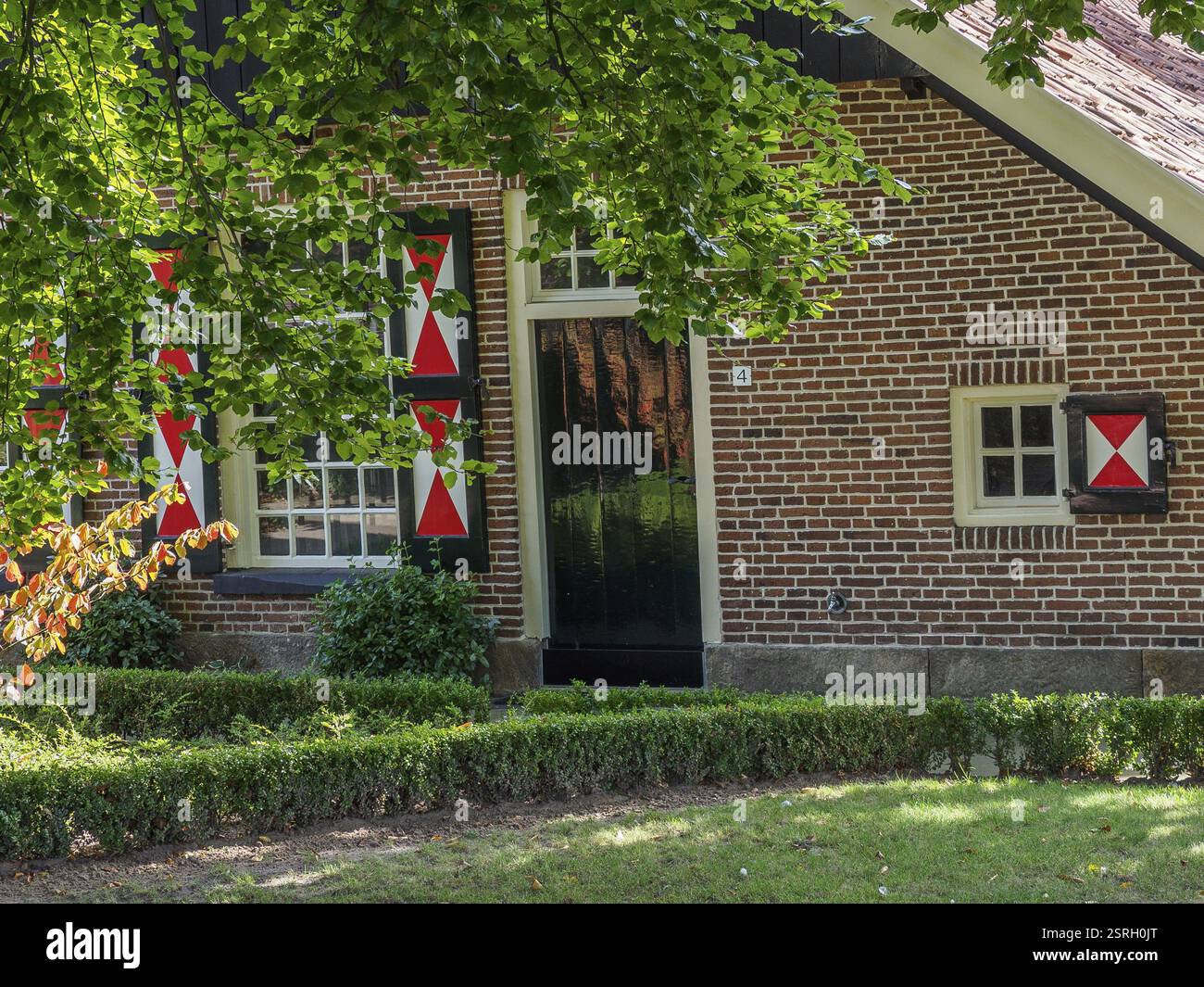 Traditional brick house with red and white shutters in green ...