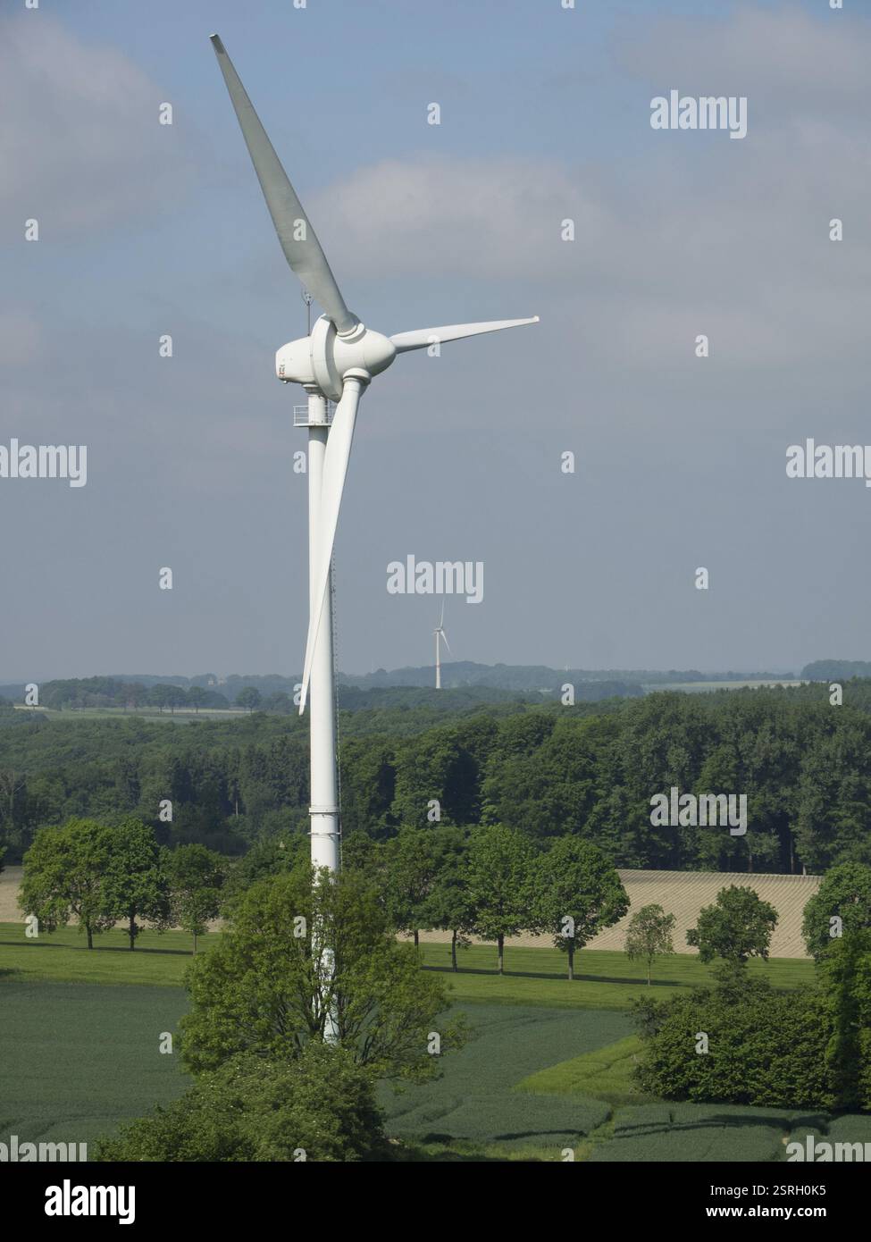Large wind turbine in a green landscape with trees and blue sky ...