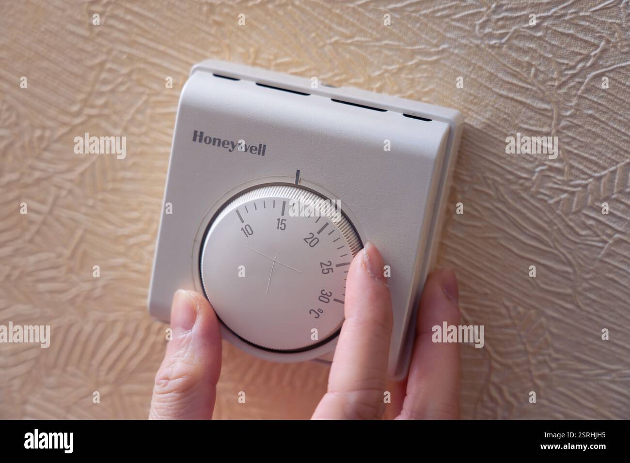 A woman's hand turning a temperature dial on a Honeywell thermostat in ...