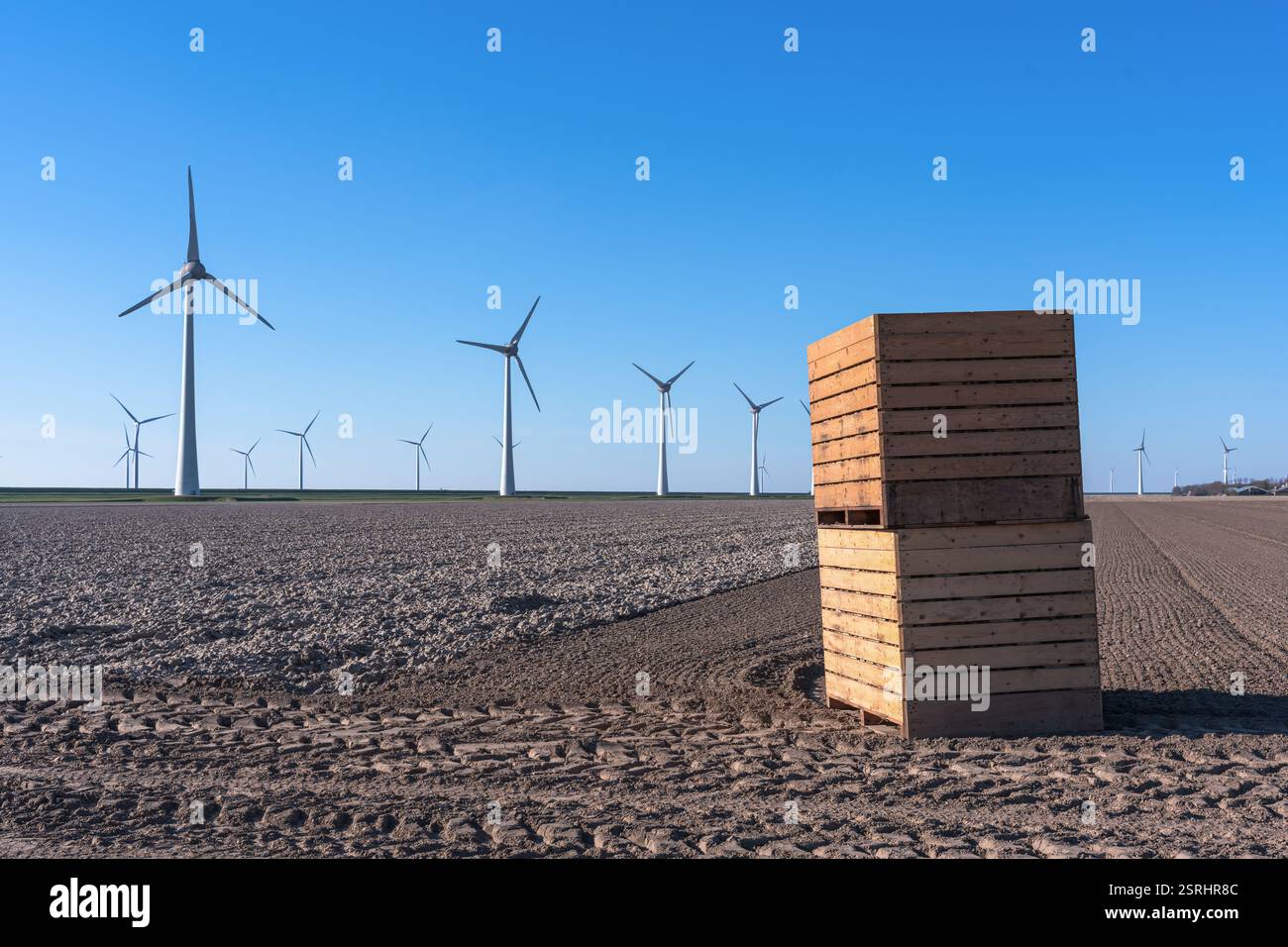 A plowed farmland with wooden crates, wind turbines in the distance ...