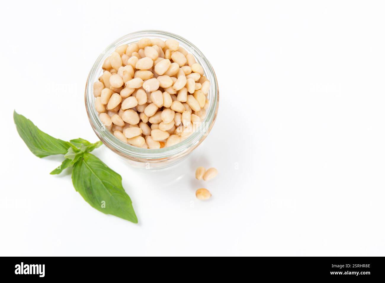 A jar of pine nuts with fresh basil leaves on white background, great ...