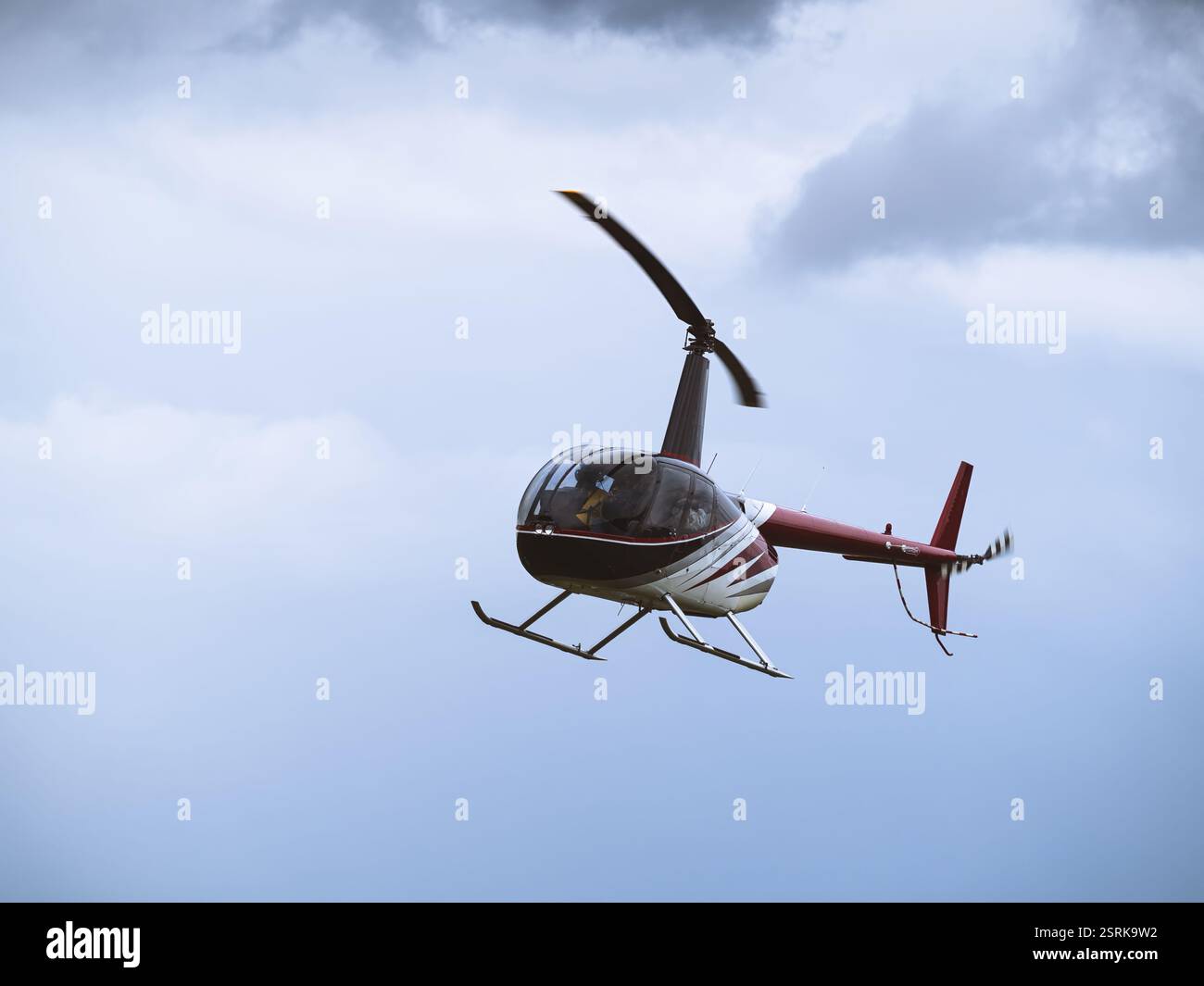 A red and white helicopter flies against a cloudy sky. The rotor blades ...