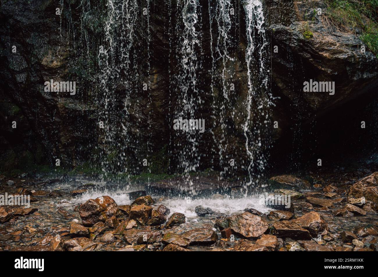 A cascading waterfall flows over a rugged rock formation, splashing ...