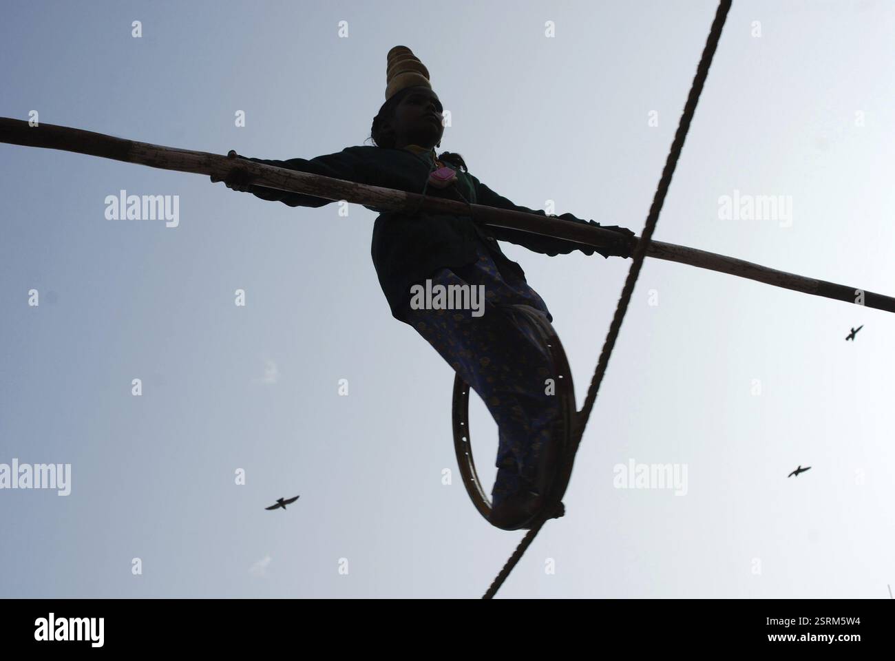 Girl balancing with bamboo in hand and stone heap on head on rope ...
