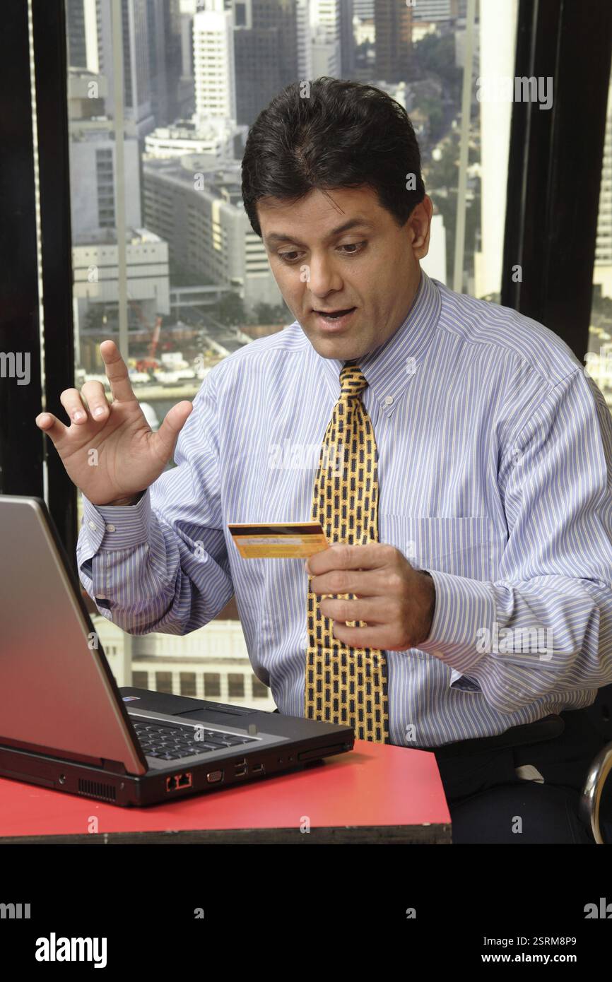 Executive with laptop and looking at credit card in office at top ...