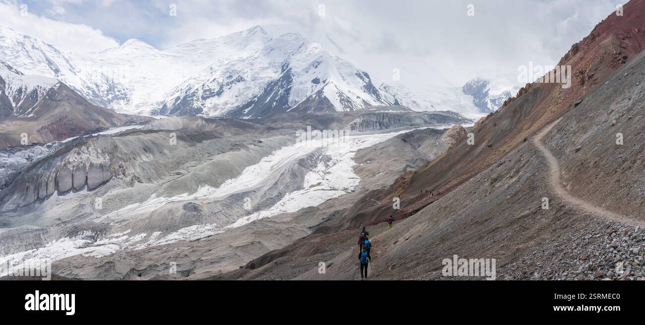 Wide panorama of valley glacier and snowy peaks with tourists hiking ...