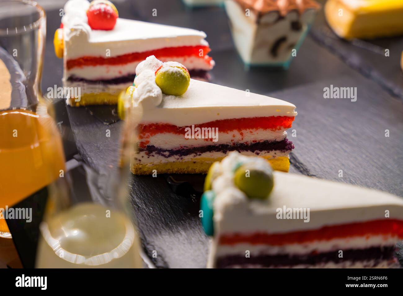 Assorted layered cakes with whipped cream and macarons on a slate ...