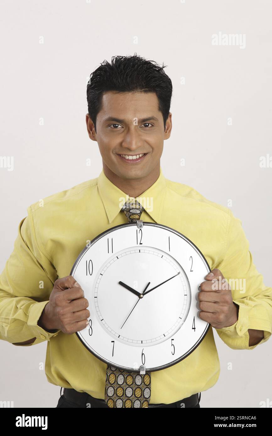 Businessman holding wall clock in both hands in front of his chest MR ...