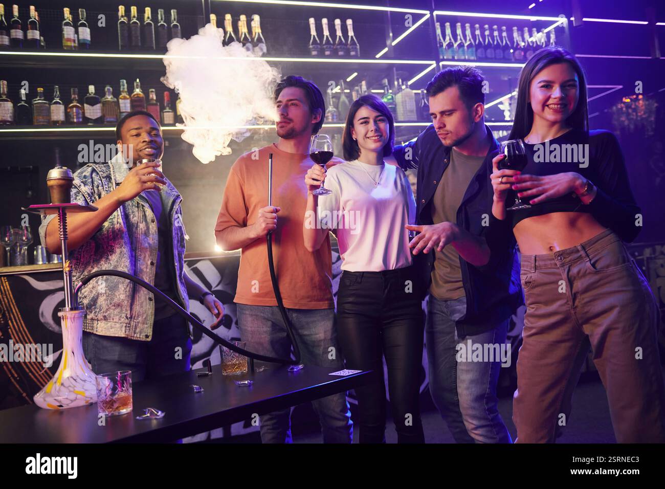 Standing near the table with hookah. Group of friends having fun in the ...