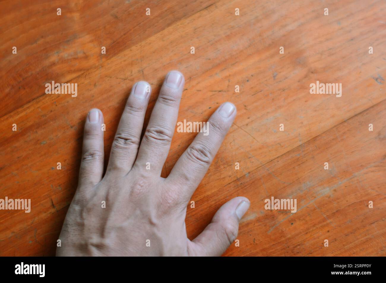 A hand rests on a warm-toned wood surface, the fingers gently spread ...