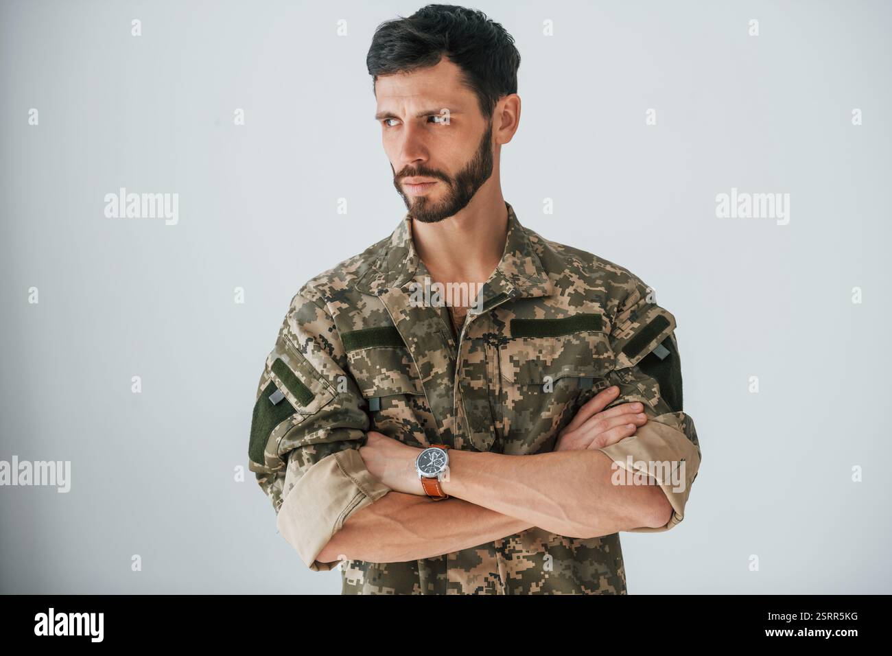 Arms crossed. Soldier in uniform is standing indoors against white wall ...