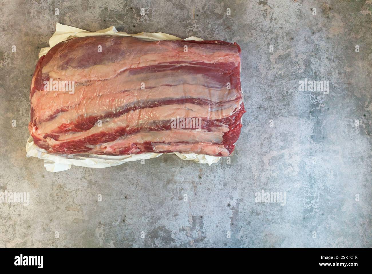 A whole, fresh, raw beef ribeye joint sits on a marble table ...