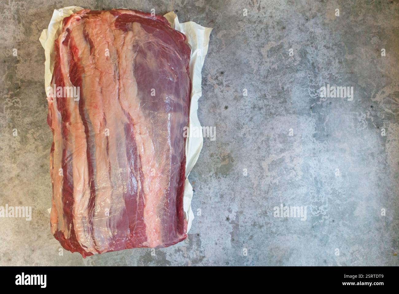 A fresh, whole raw beef ribeye joint resting on a marble table with ...