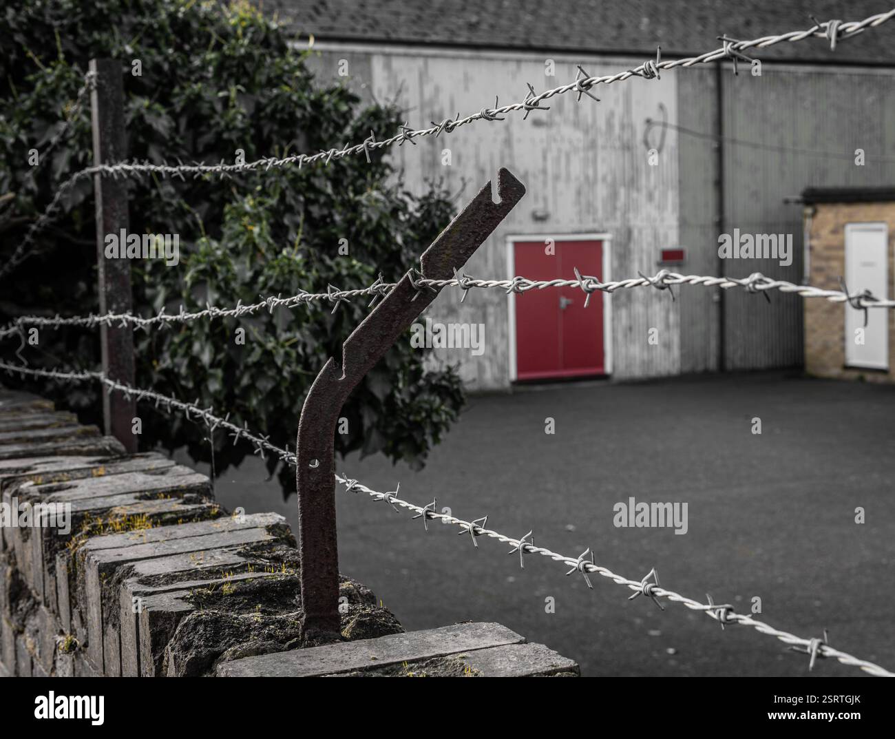 Barbed wire fence in front of a warehouse with red door. This border is ...