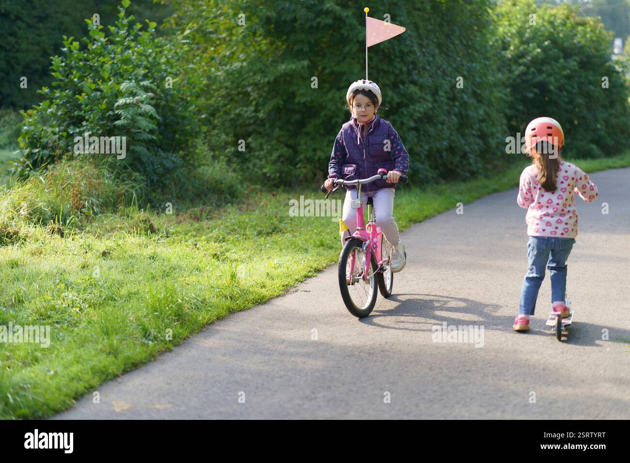 Two girls in helmets riding a bicycle and a scooter in summer. Concept ...