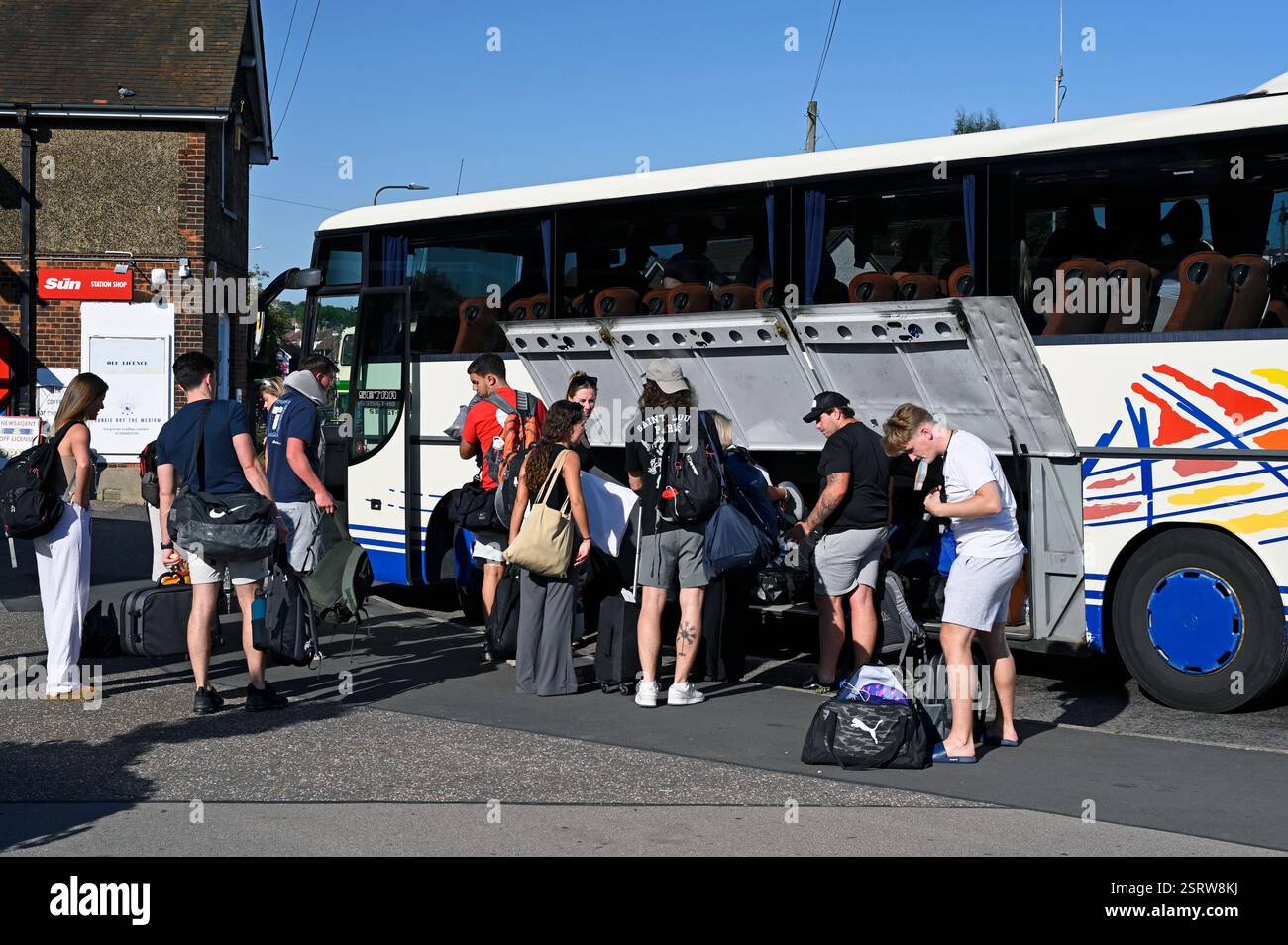 People loading luggage into the side of a coach outside the railway ...