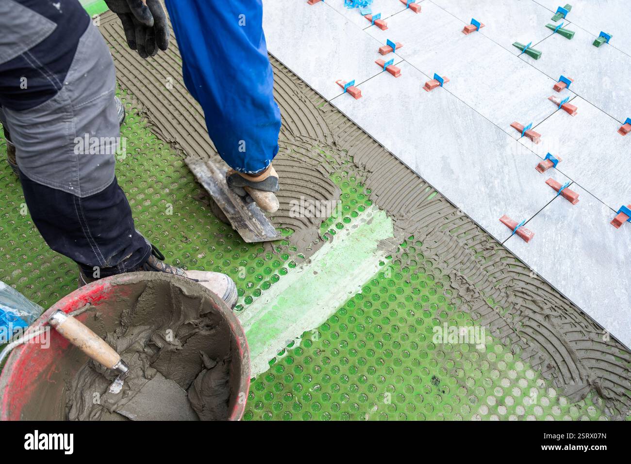 Bricklayer tiler spreads glue with notched trowel to install tiles for ...