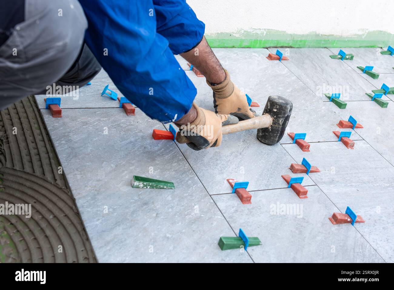 Bricklayer tiler with hammer puts in place the tiles of a new floor ...