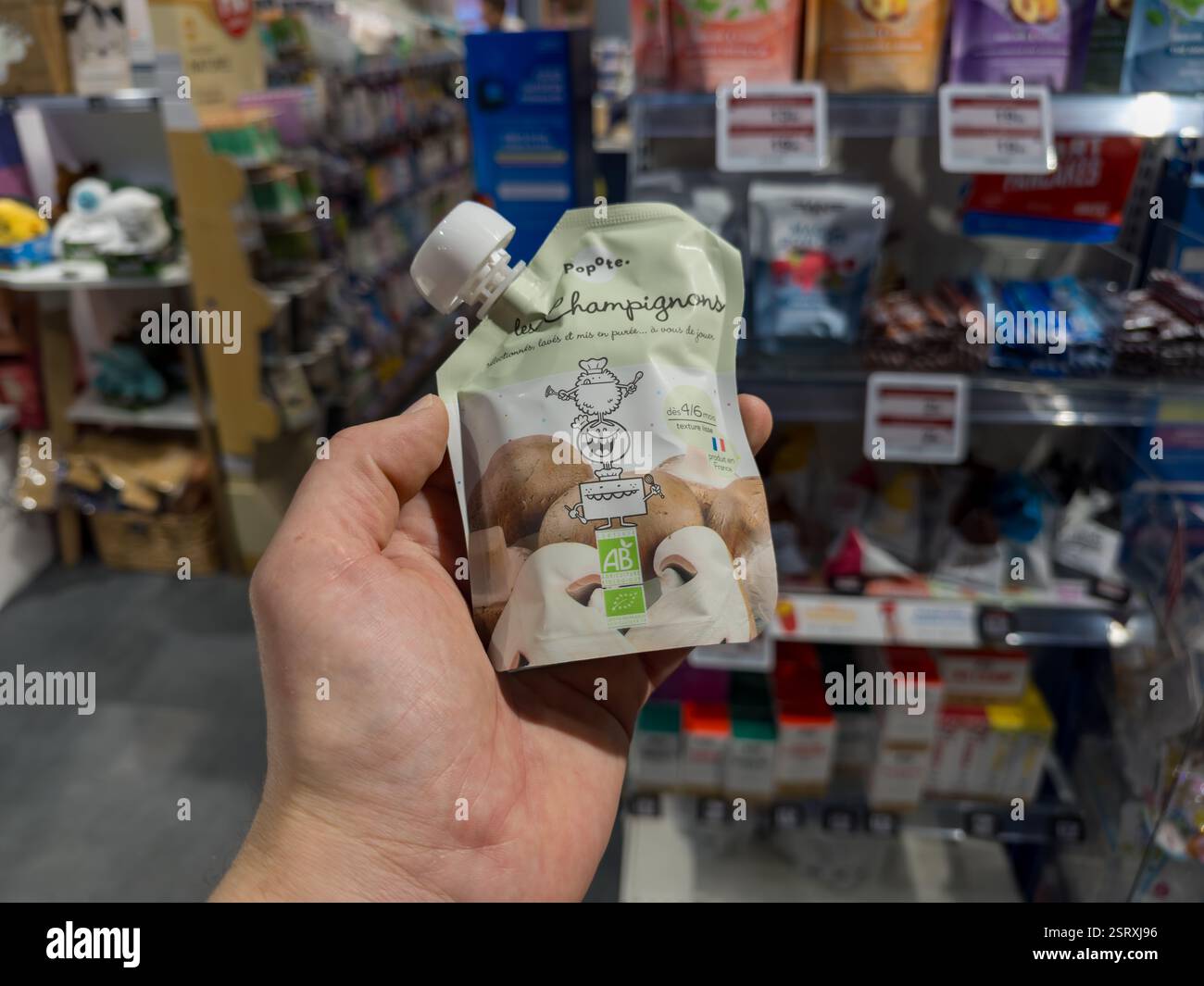 Hand holding a pouch of gourmet mushroom puree in a vibrant store aisle ...