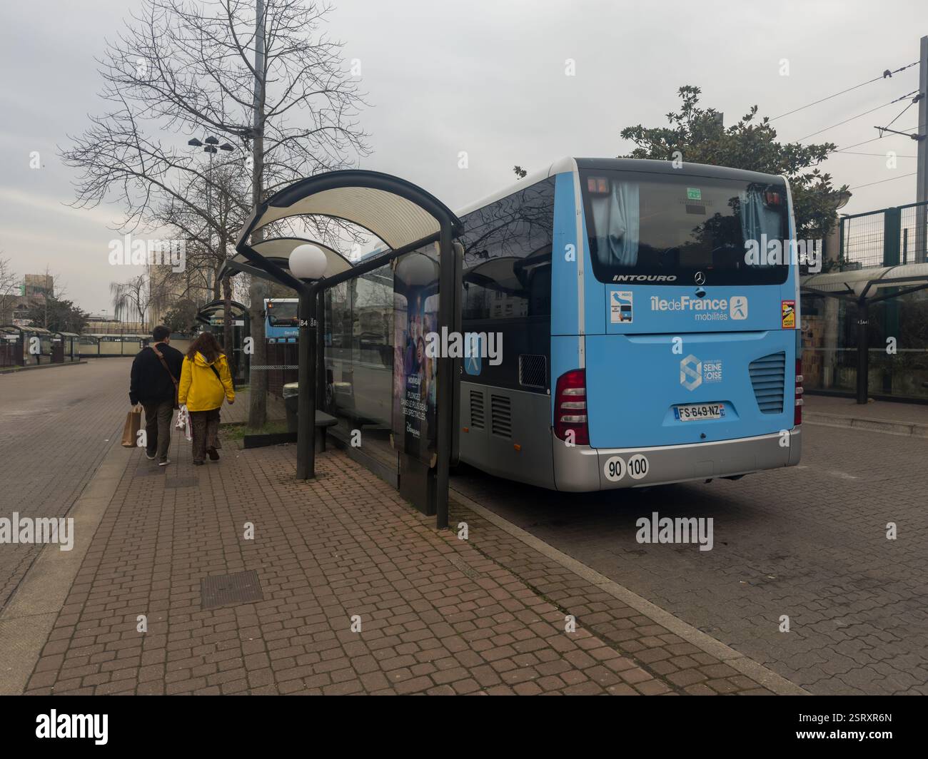 Two people walk towards a bus stop where a blue urban bus stands ready ...