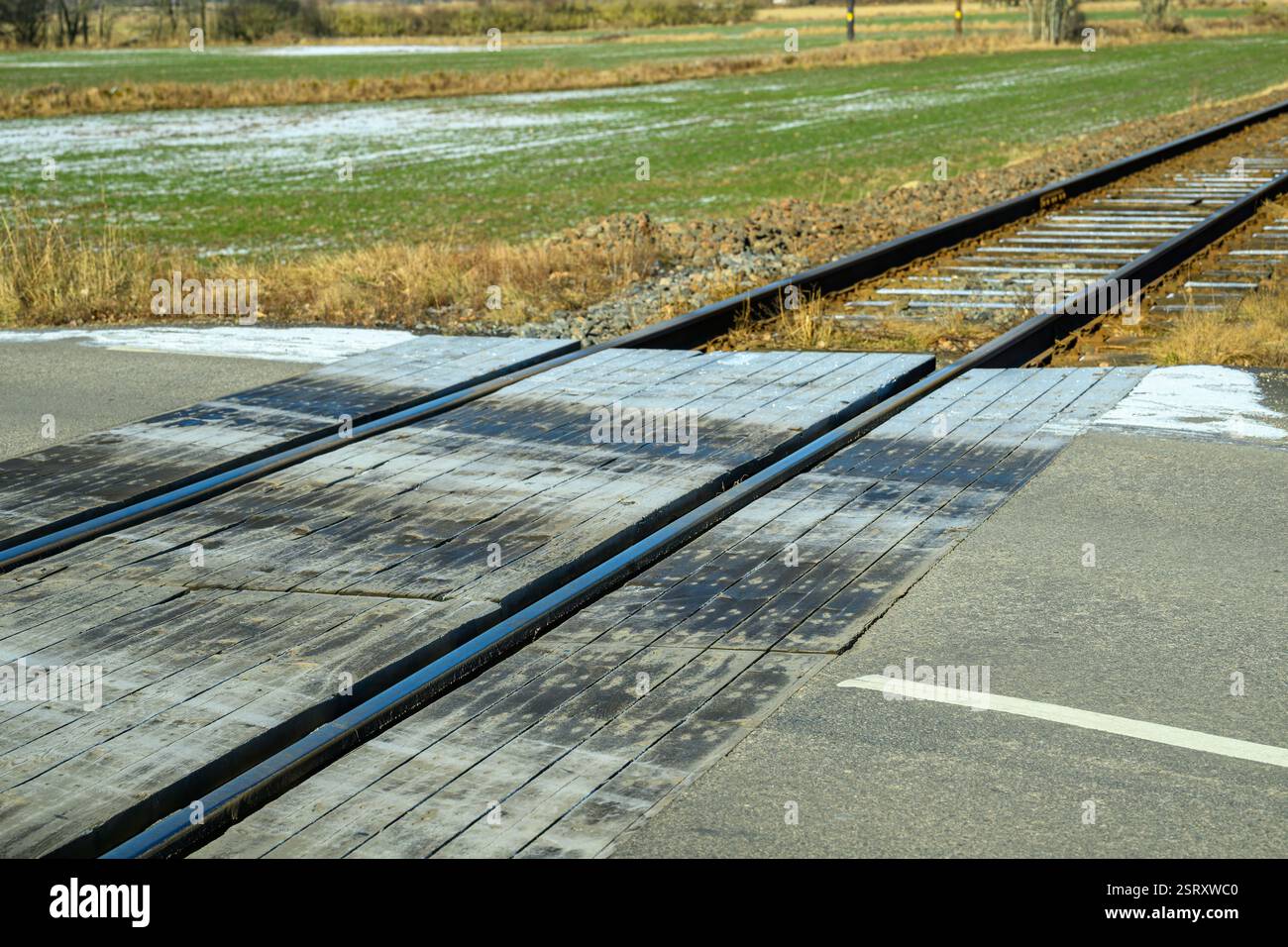 A railway crossing is visible at a rural road, surrounded by open grassy fields under a clear ...