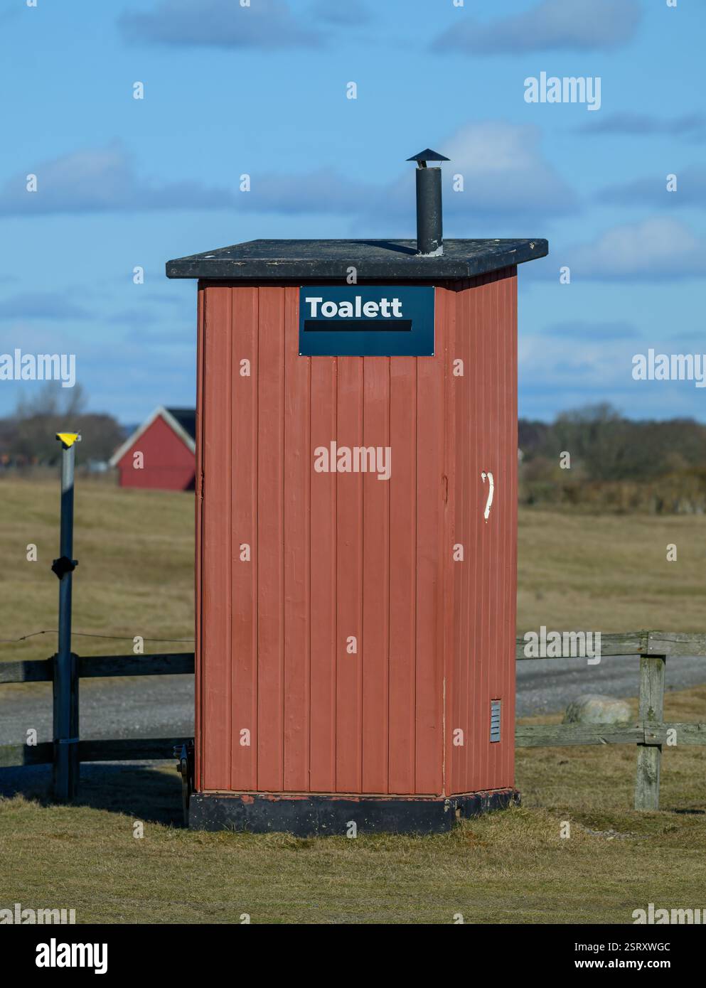 A bright red outdoor toilet stands alone in a vast, open field. The ...