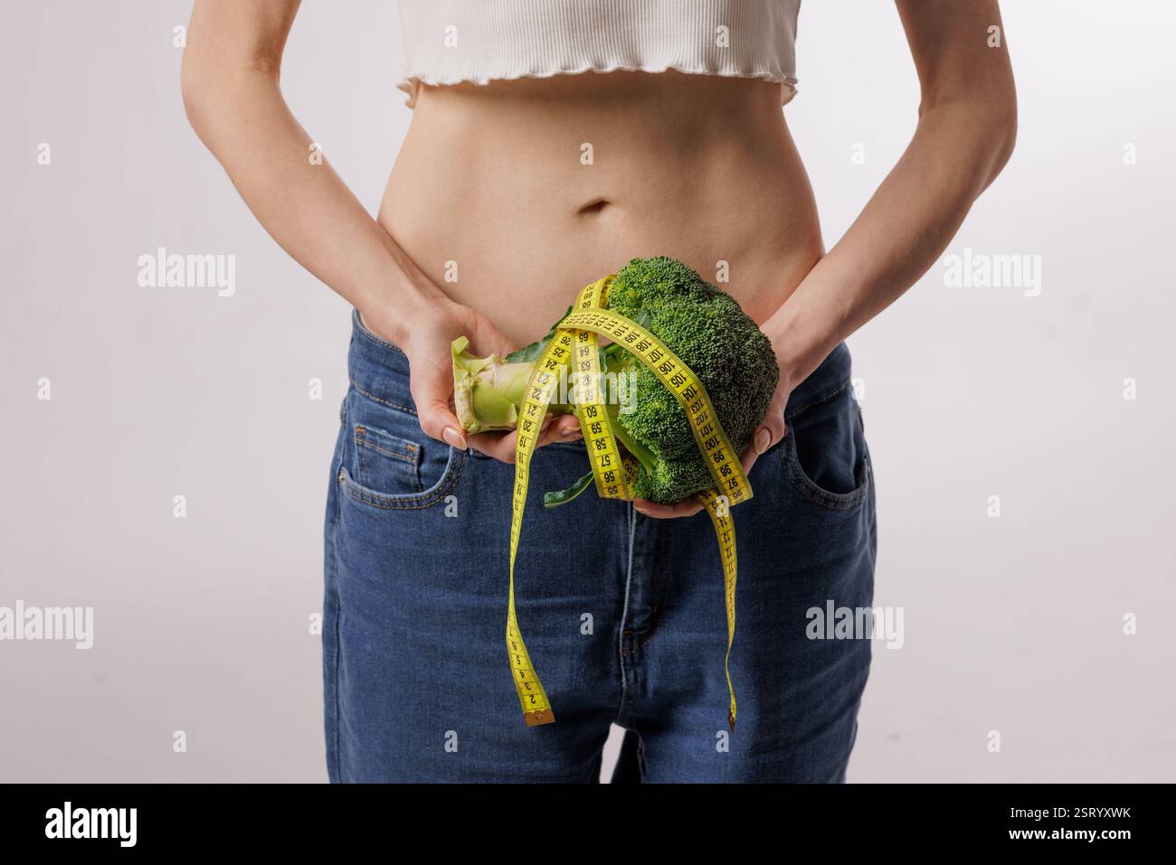 Slim woman holding broccoli wrapped in a measuring tape, symbolizing ...