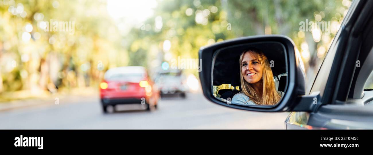 Happy beautiful middle-aged woman in the rearview mirror of her new car ...