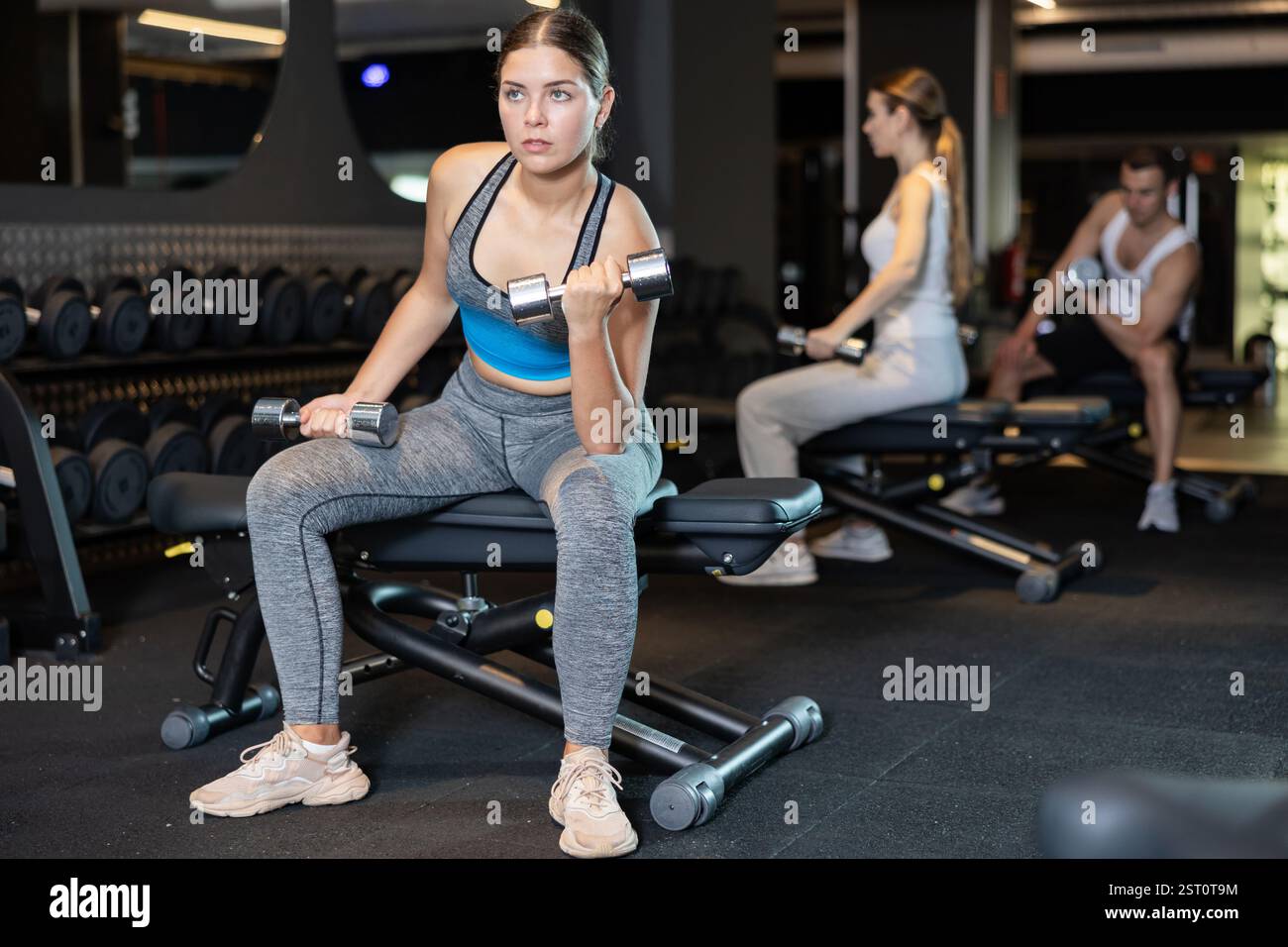 Slender girl trains muscles of arms and back using dumb-bell shaped ...