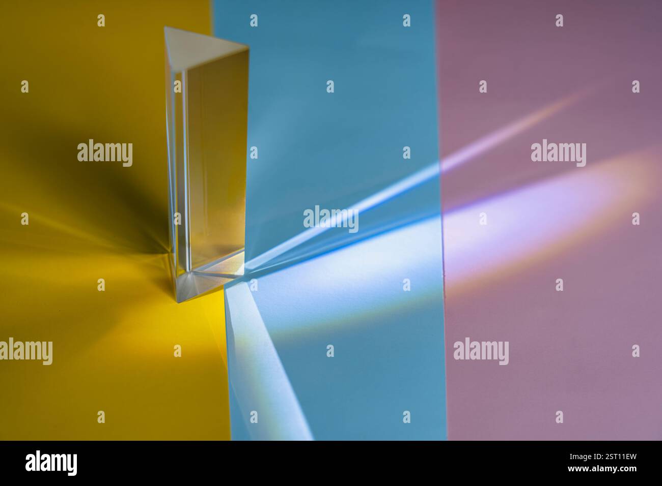 Transparent glass prism placed on yellow, blue, and pink paper ...