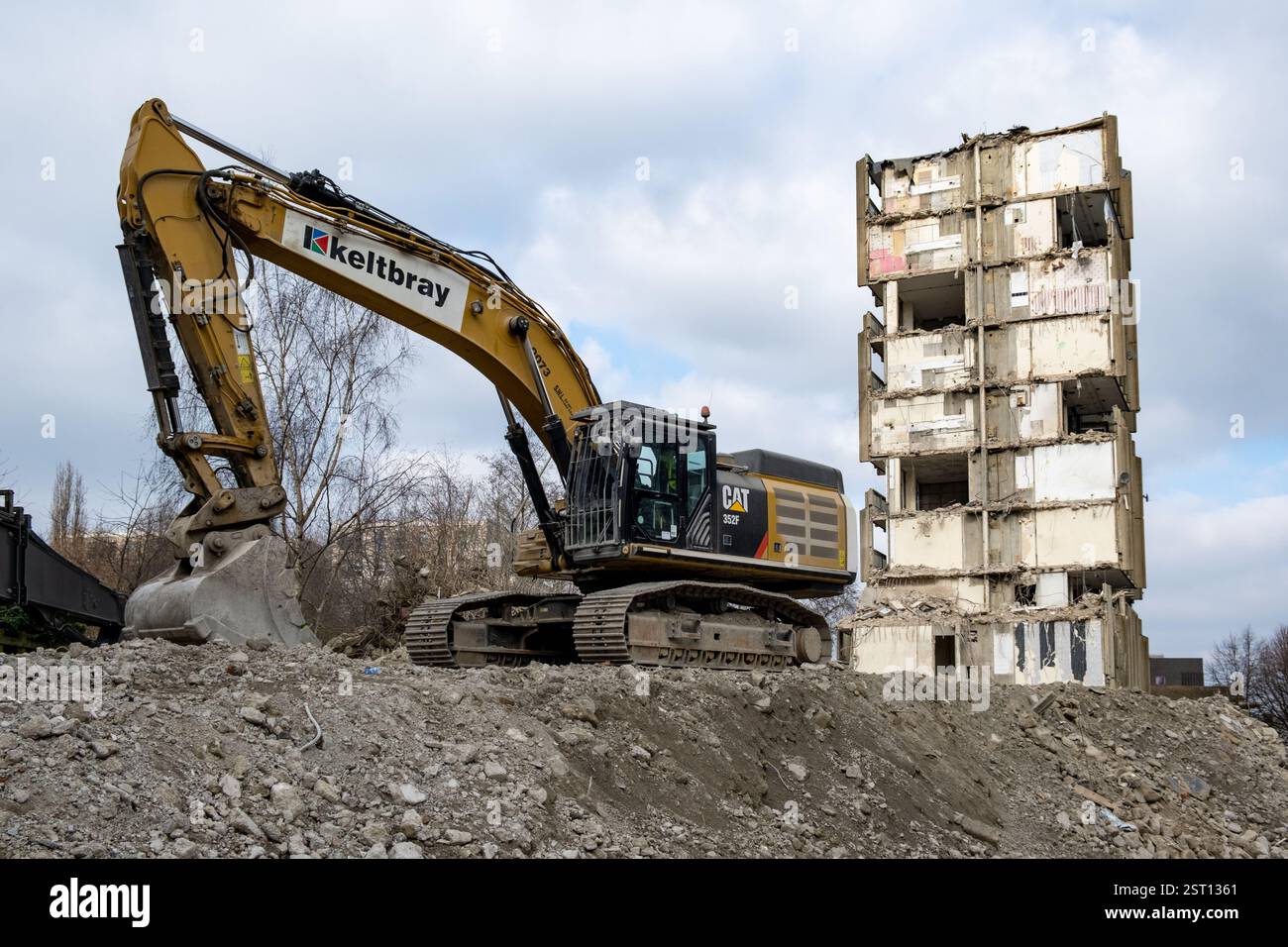 A digger sits on a pile of rubble in front of half demolished tower ...