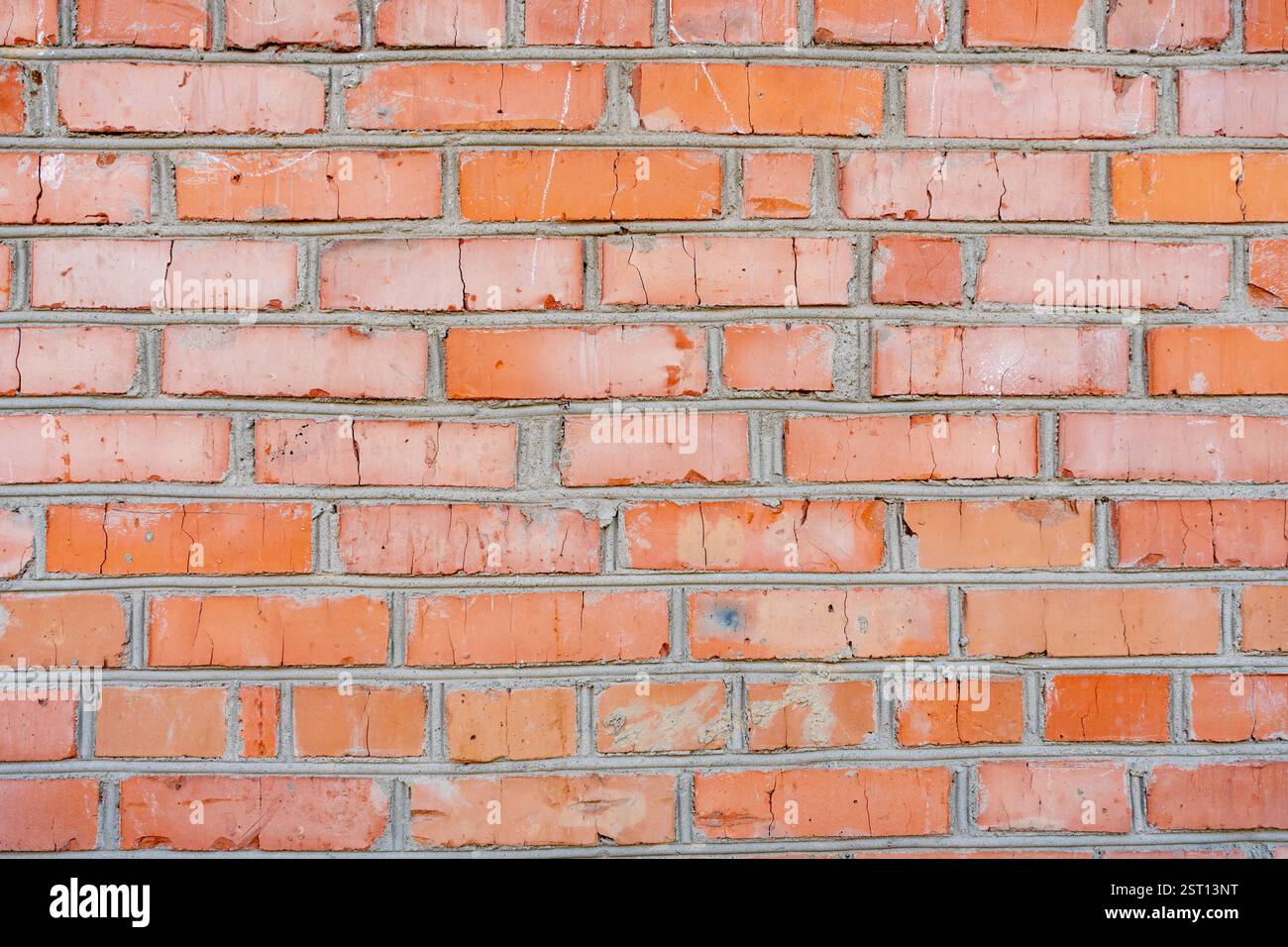 A weathered red brick wall showcases various shades and textures. Cracks and mortar lines add ...