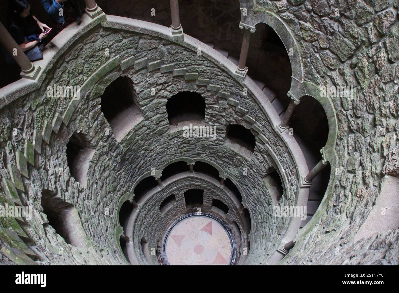 A winding stone spiral staircase plunges into a shadowy well. A ...