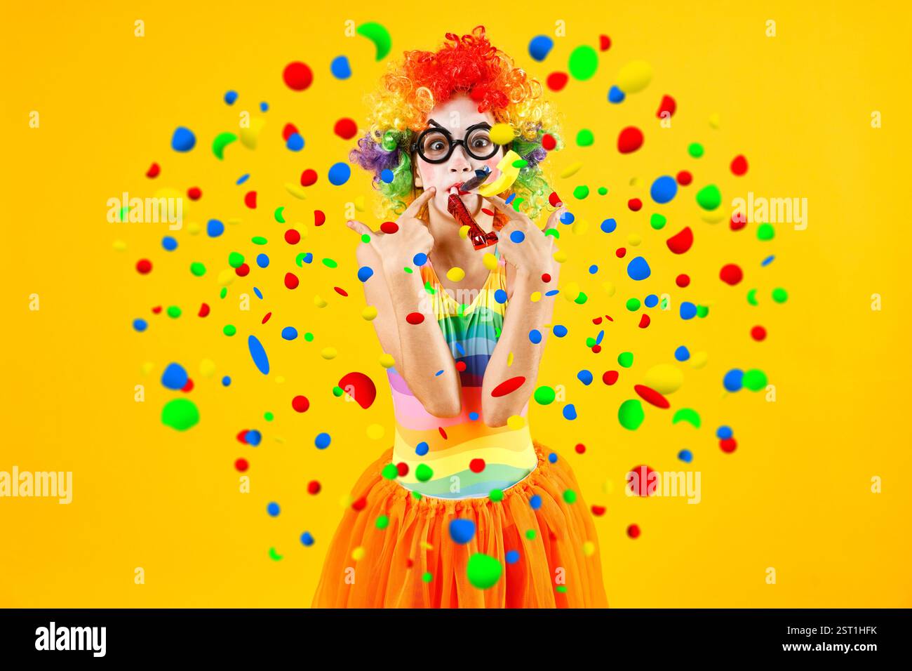 Girl dressed like clown with party blowers under falling confetti on ...