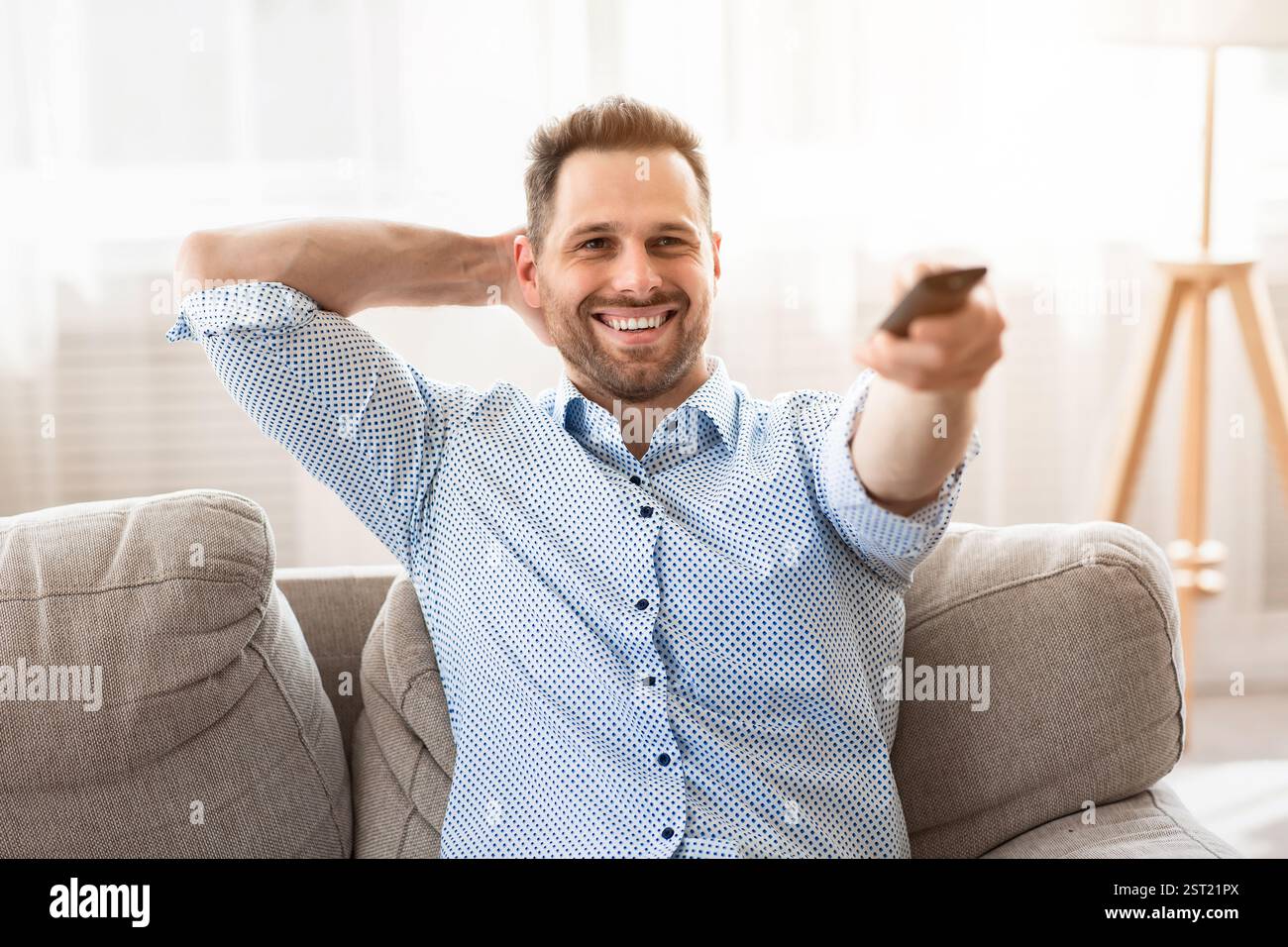 Happy guy watching TV at home, holding remote control Stock Photo - Alamy