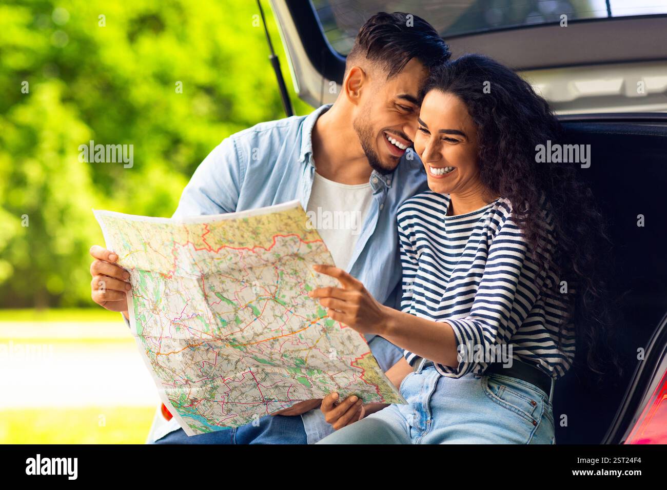 Happy lovers cuddling while sitting on trunk and watching map Stock Photo - Alamy